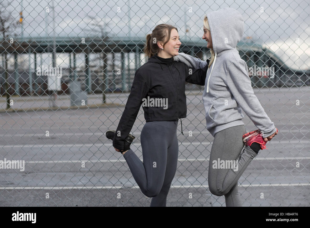 Two female runner friends stretching legs by wire fence Stock Photo - Alamy