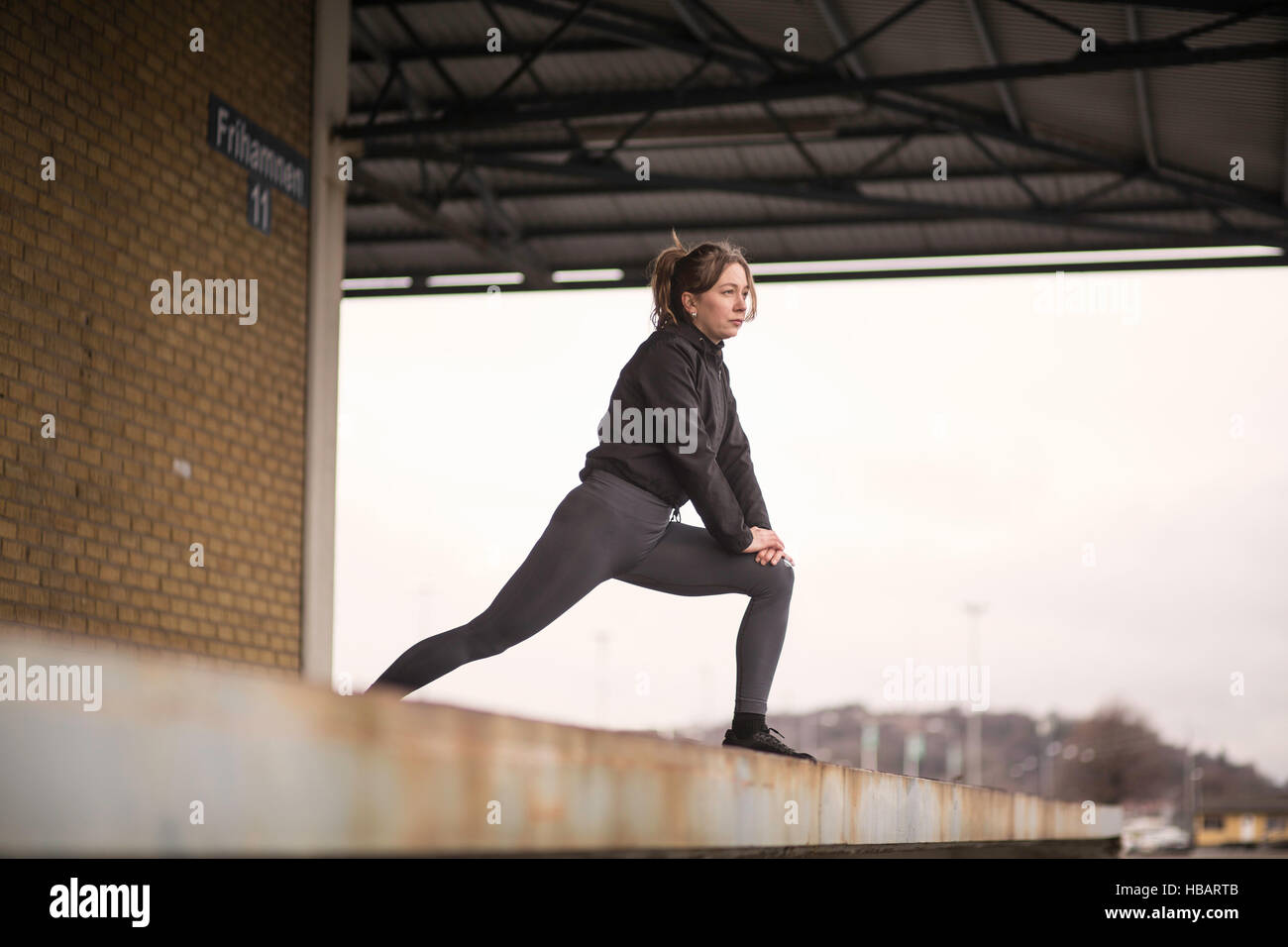 Female runner leaning forward stretching on warehouse platform Stock ...