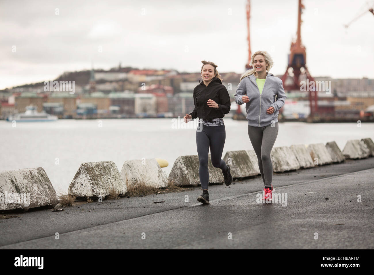 Two female runner friends running along dockside Stock Photo - Alamy
