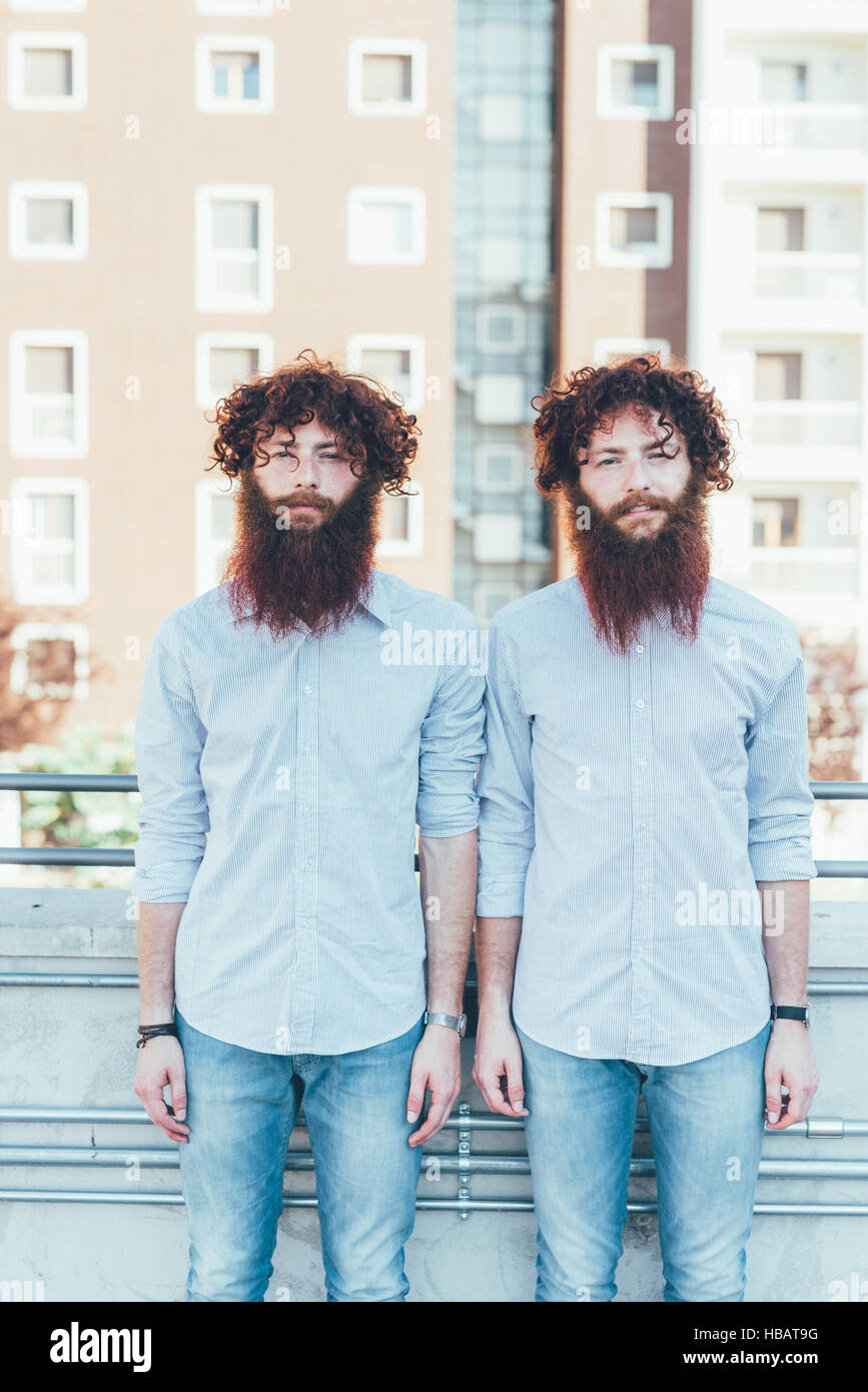 Portrait of identical male hipster twins standing on apartment roof ...