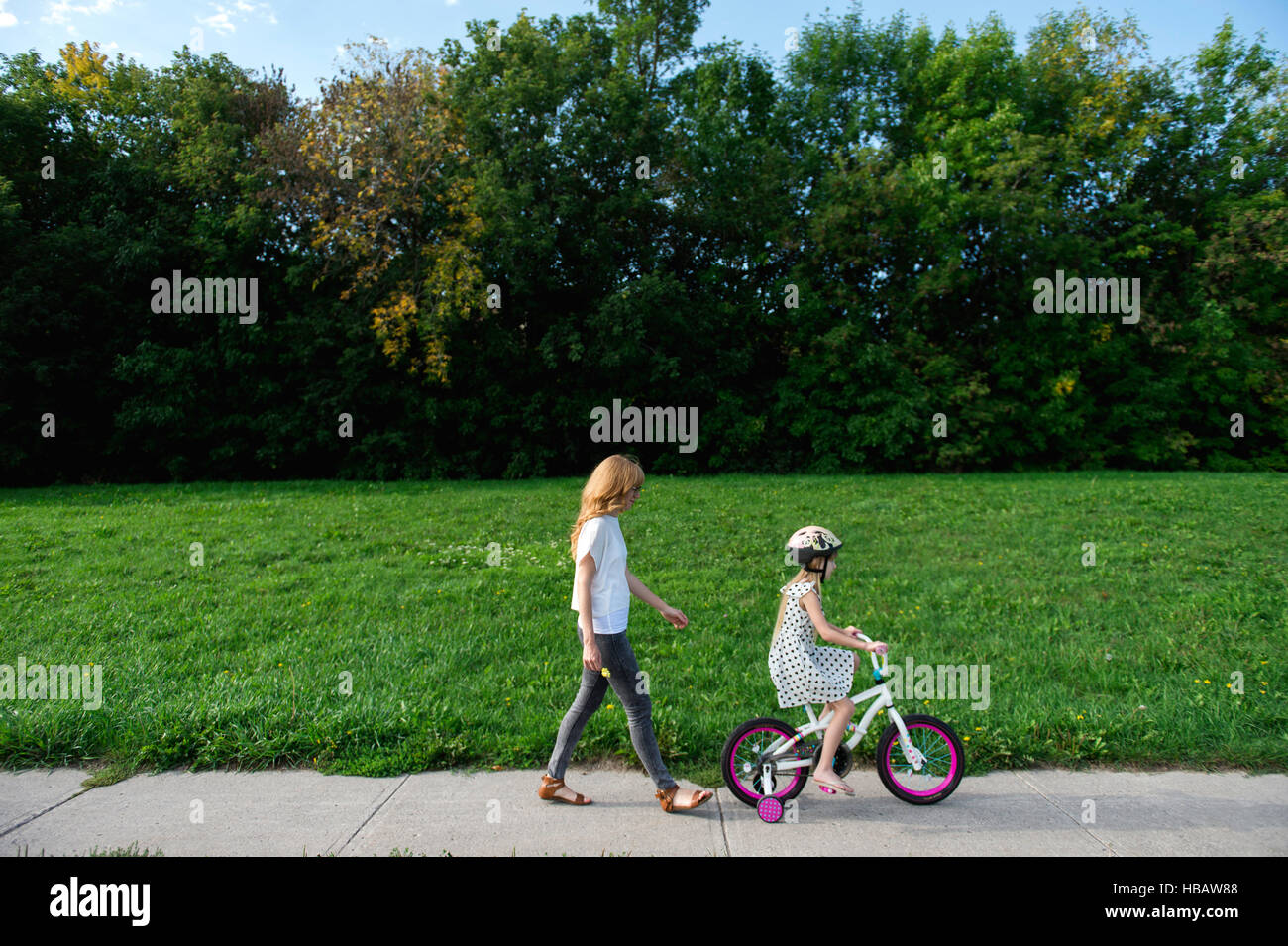 Young girl riding her bicycle followed by mother Stock Photo - Alamy