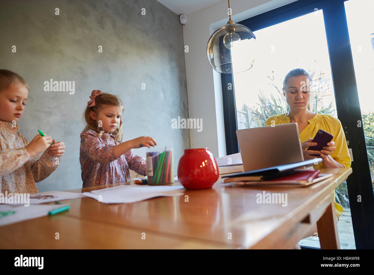 Mid adult woman reading smartphone texts at dining table whilst ...