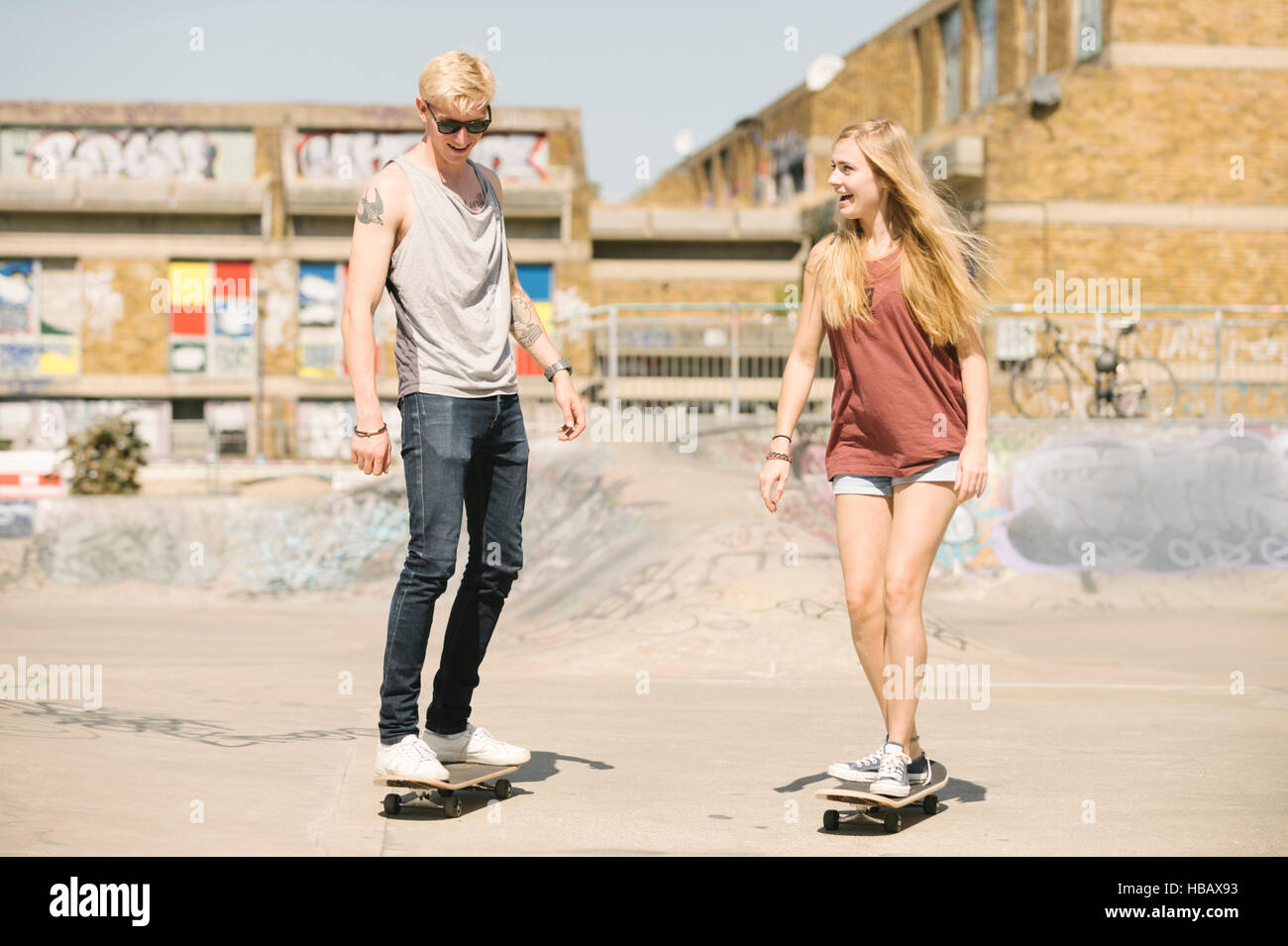Young female and male skateboarding friends skateboarding in skatepark ...