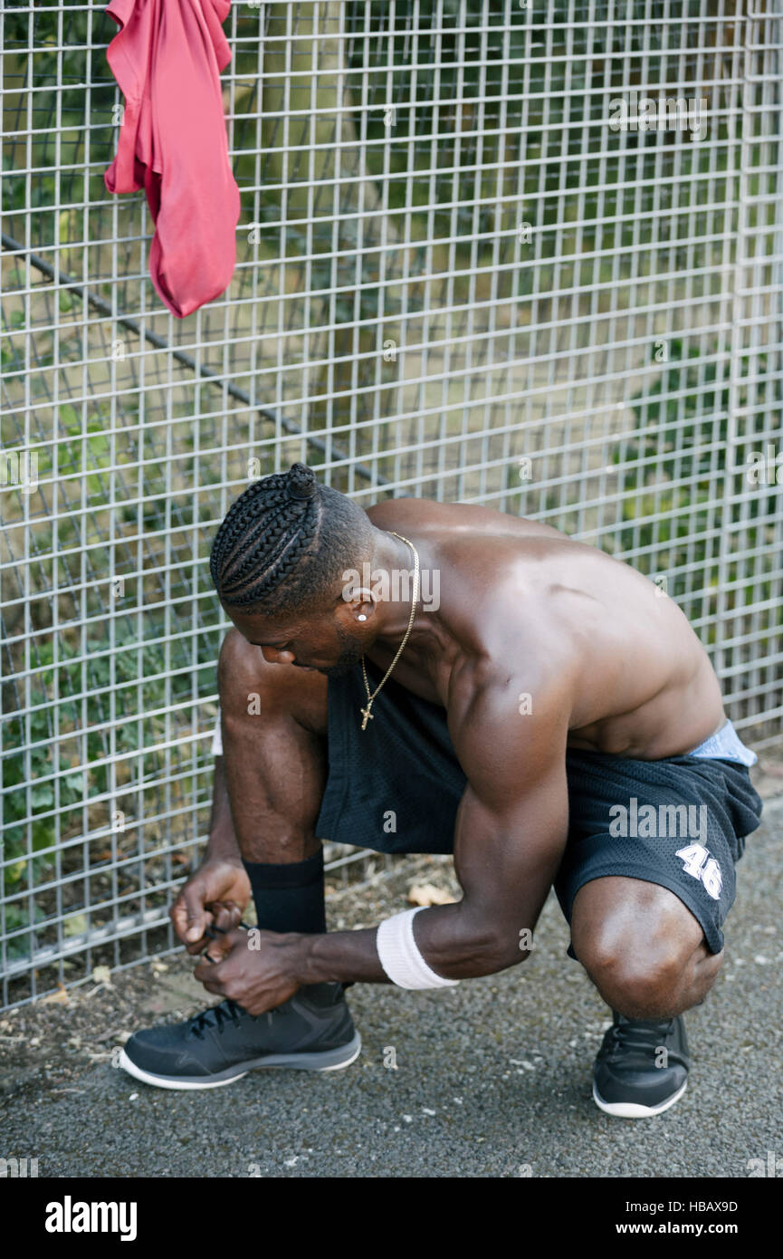 Young man tying trainer laces on basketball court Stock Photo - Alamy