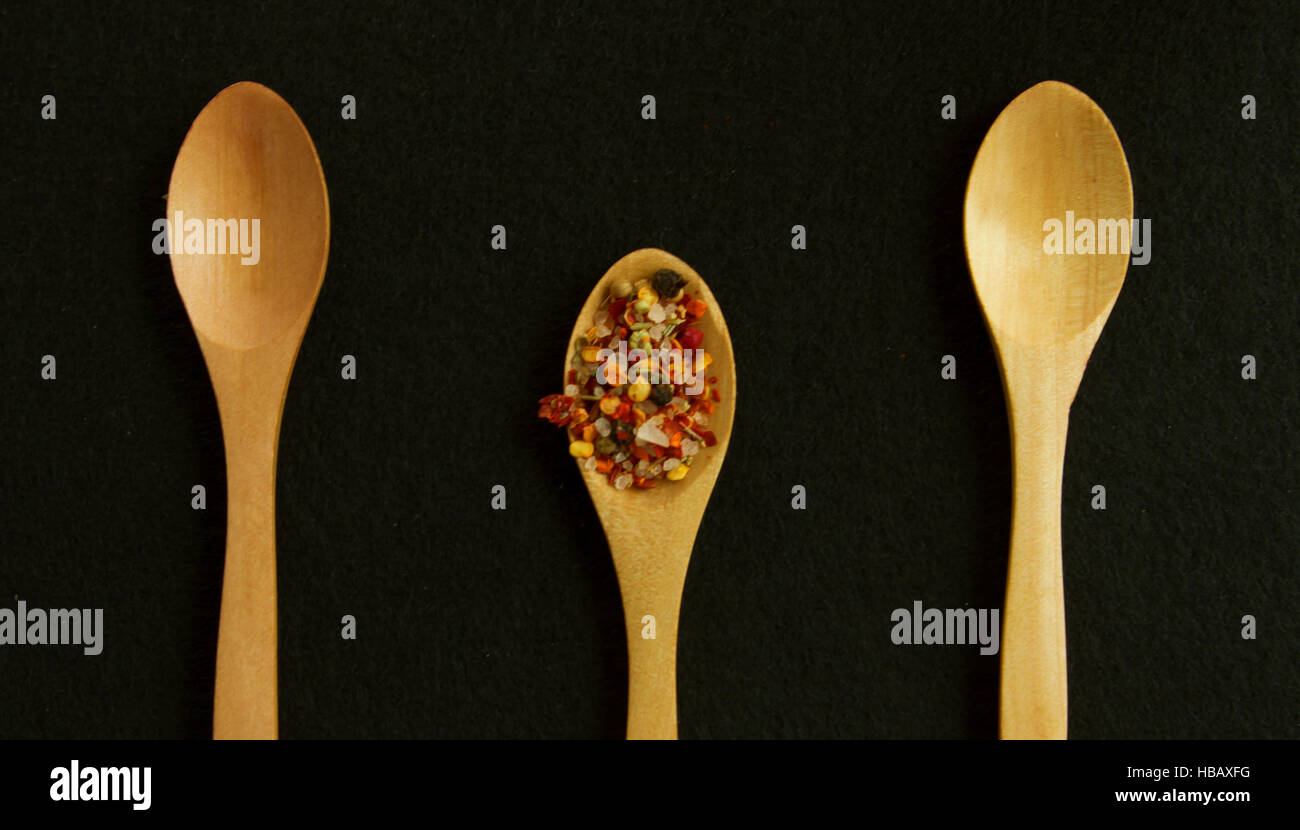 Four spoons, one with spices and three are empty on black background ...