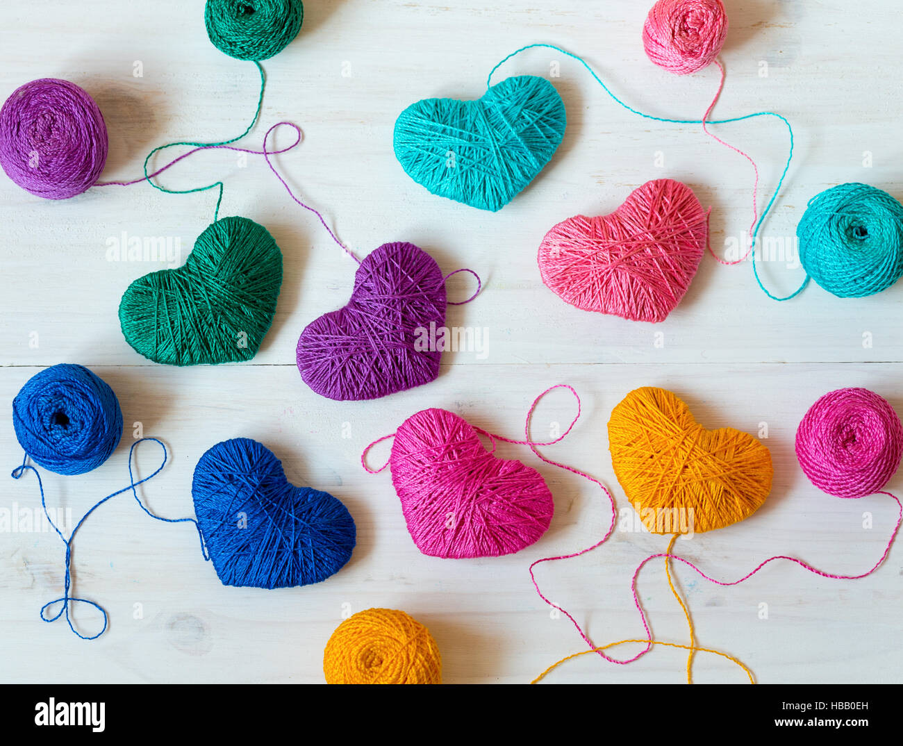 Multicolored Hearts with a balls of thread on white wooden background ...