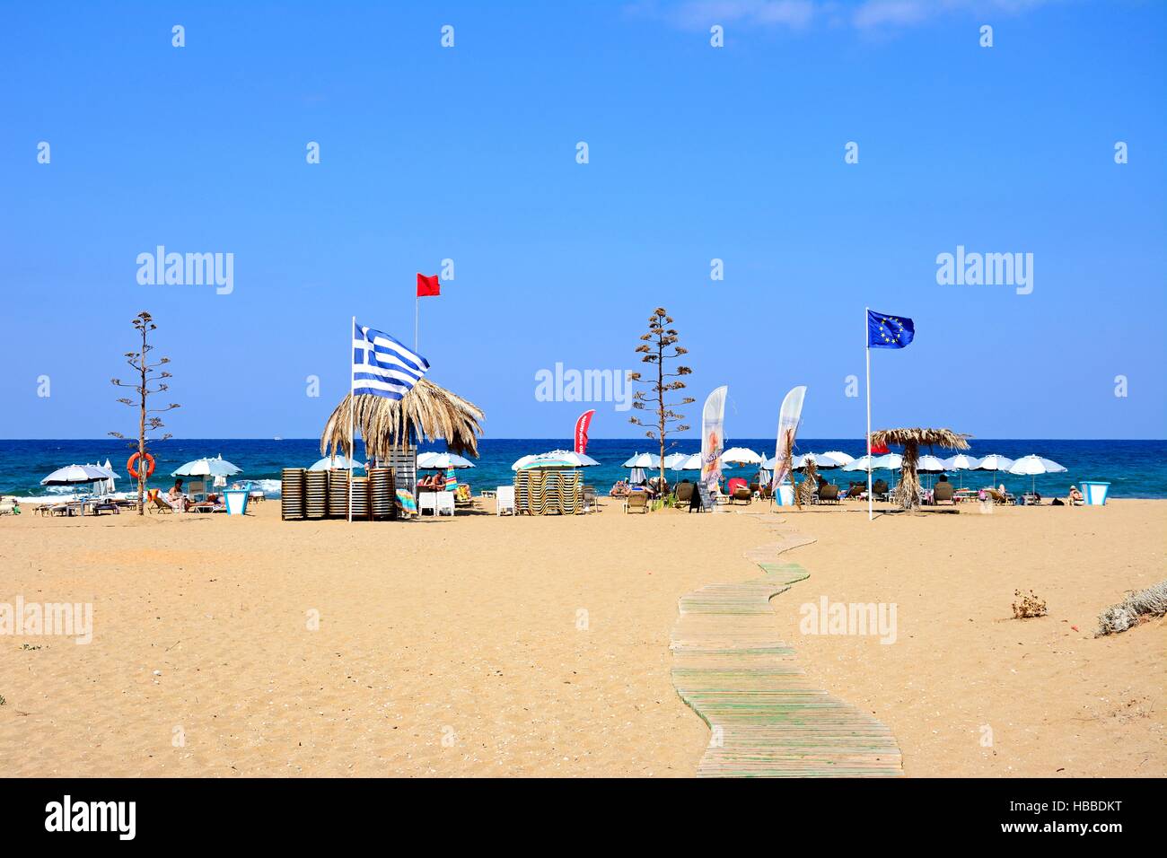 View of Potamos beach with flags and parasols and the sea to the rear ...