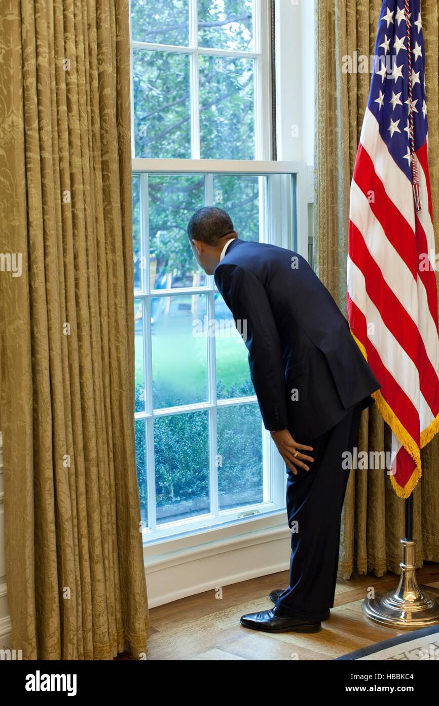 President Barack Obama looks out a window in the Oval Office to see ...