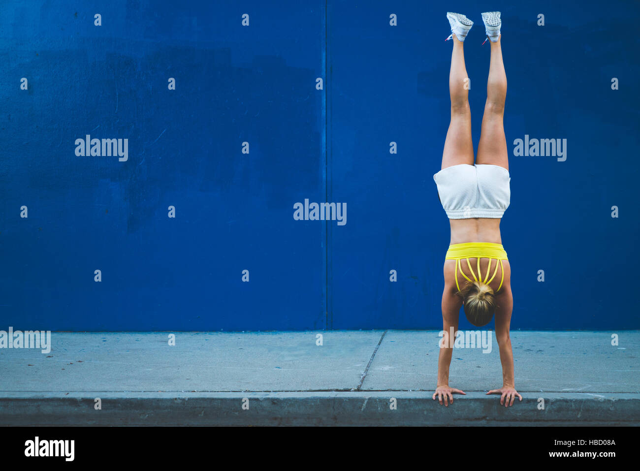 Young woman doing handstand outdoors in front of blue wall Stock Photo ...