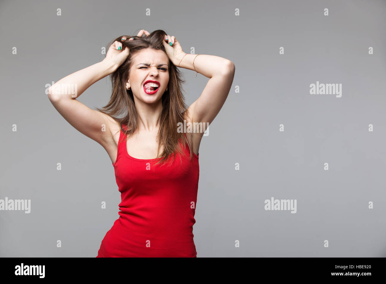 Young brunette woman showing devil horns hand gesture posing in studio ...