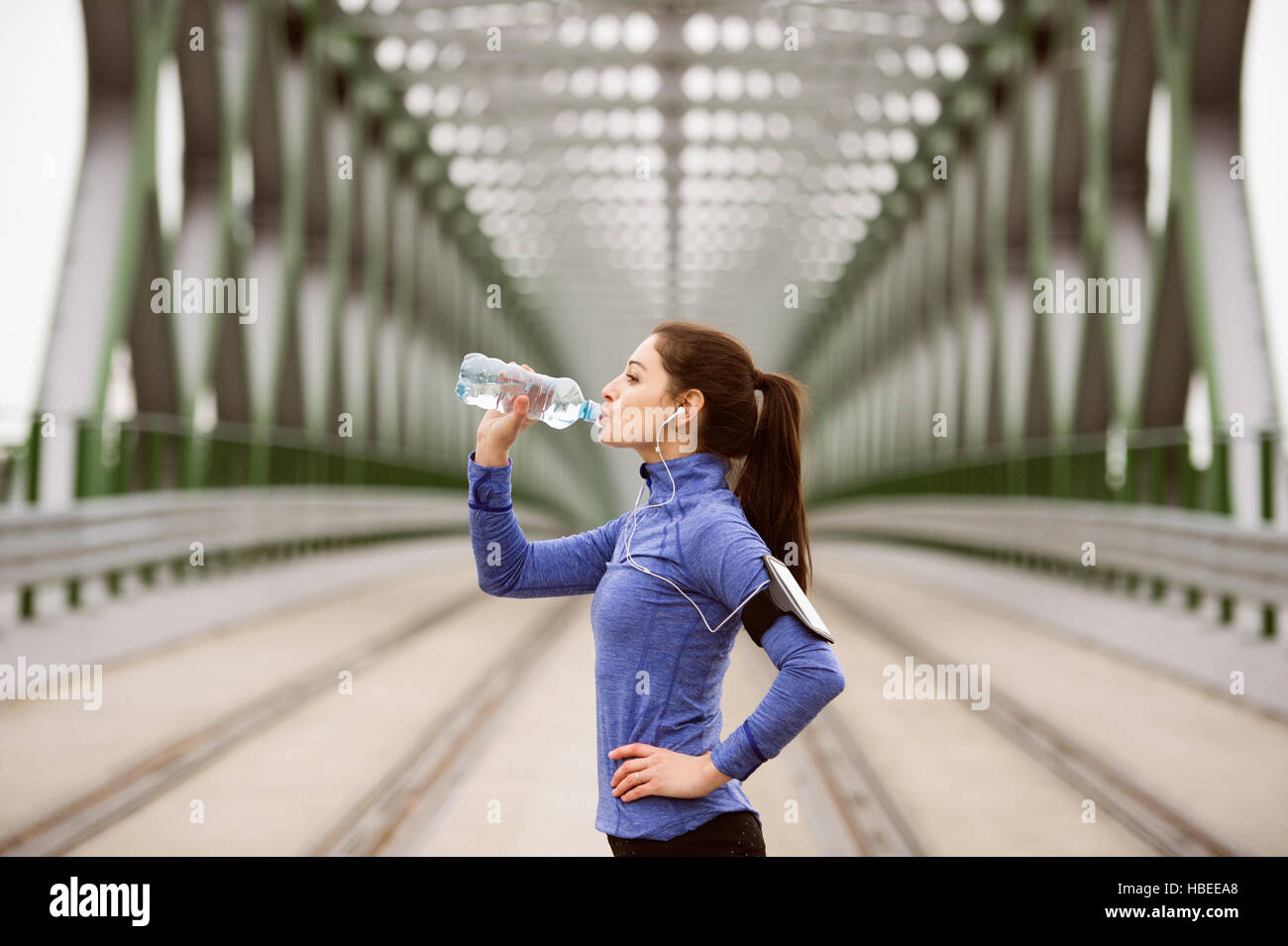 Young runner resting, drinking water on green steel bridge Stock Photo ...