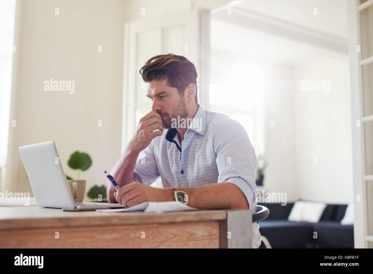 Side view shot of pensive young man sitting at home and working on ...