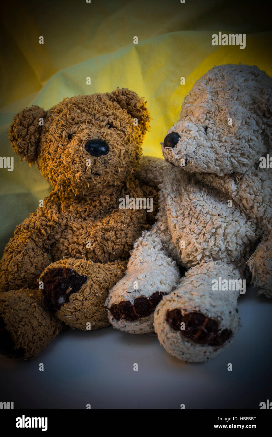 Two Teddy Bears sit embracing one another. One is smiling and the other ...