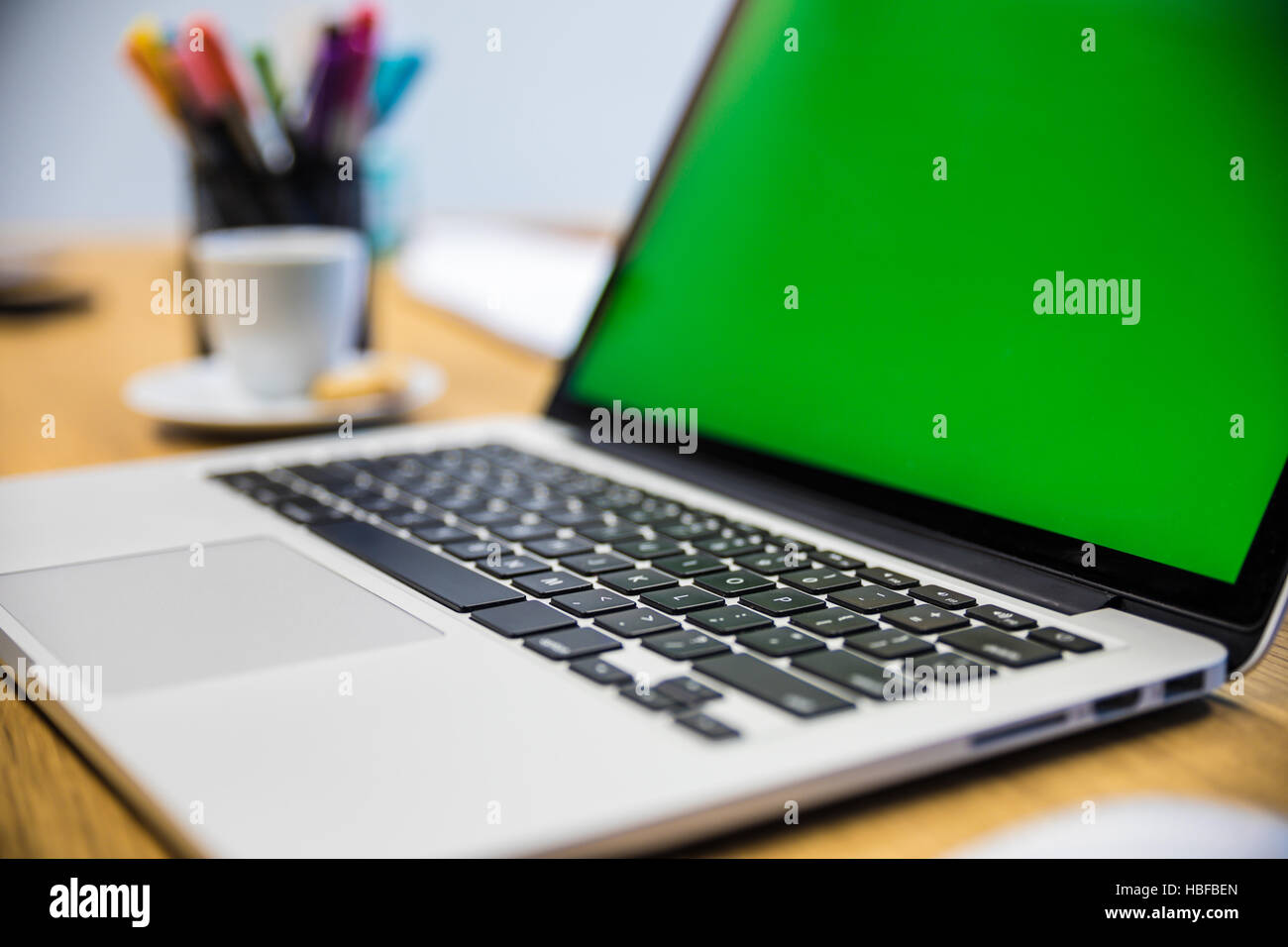 Side view of laptop with blank green screen on table in modern office ...