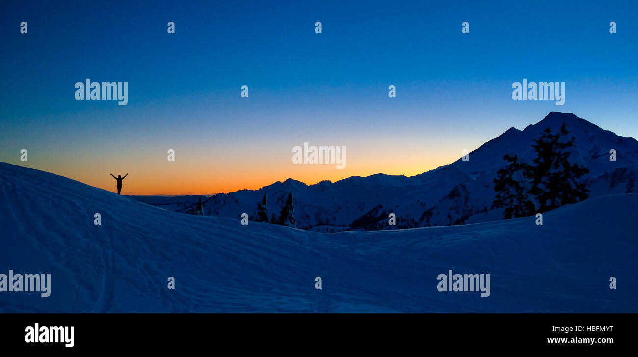A single person standing with arms raised against a wilderness sunset ...