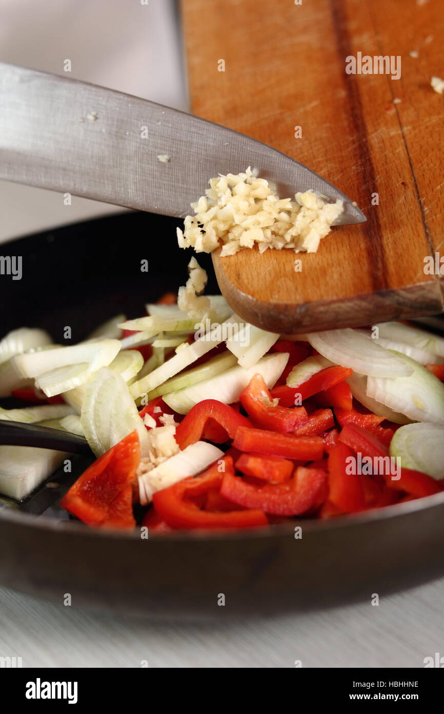Adding minced garlic into skillet with red bell pepper and onion ...