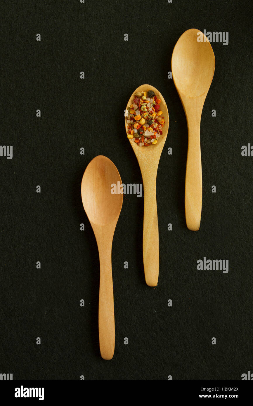 Three spoons, one with spices and two are empty on black background ...