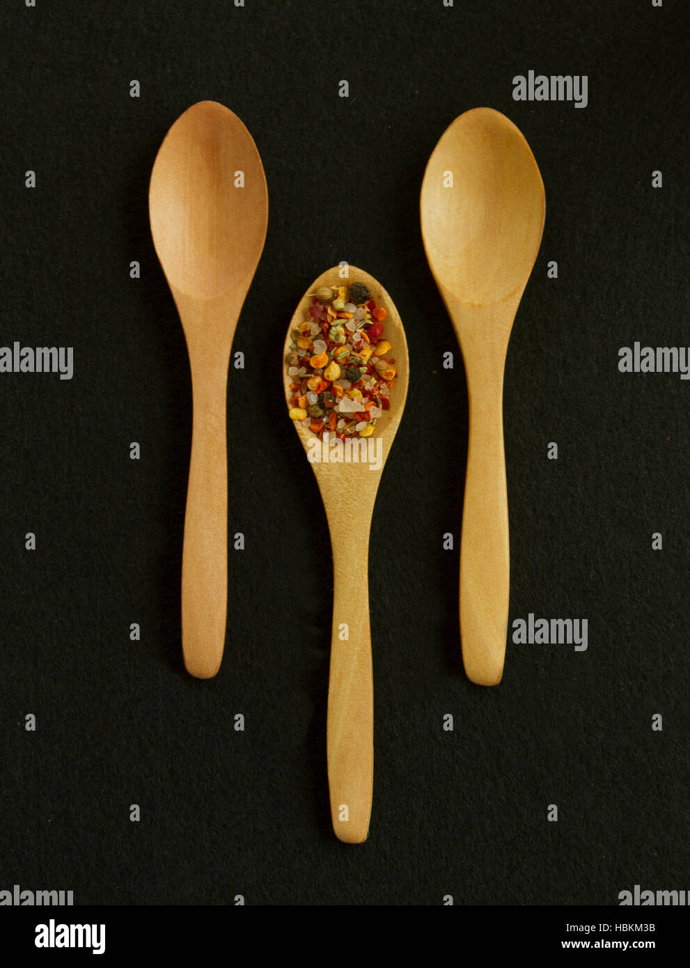 Three spoons, one with spices and two are empty on black background ...