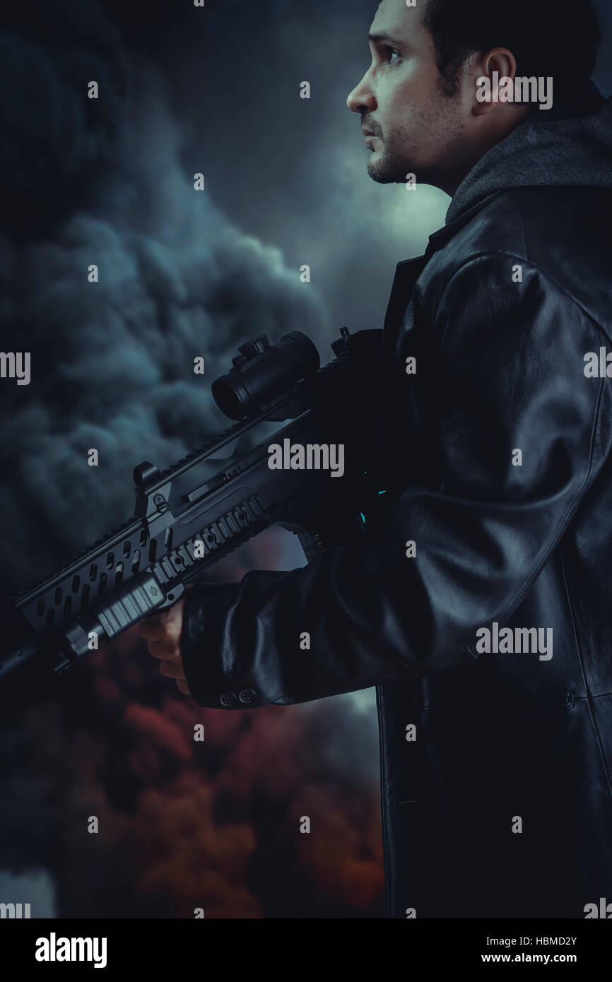 Man with long leather jacket and assault rifle, black smoke background ...