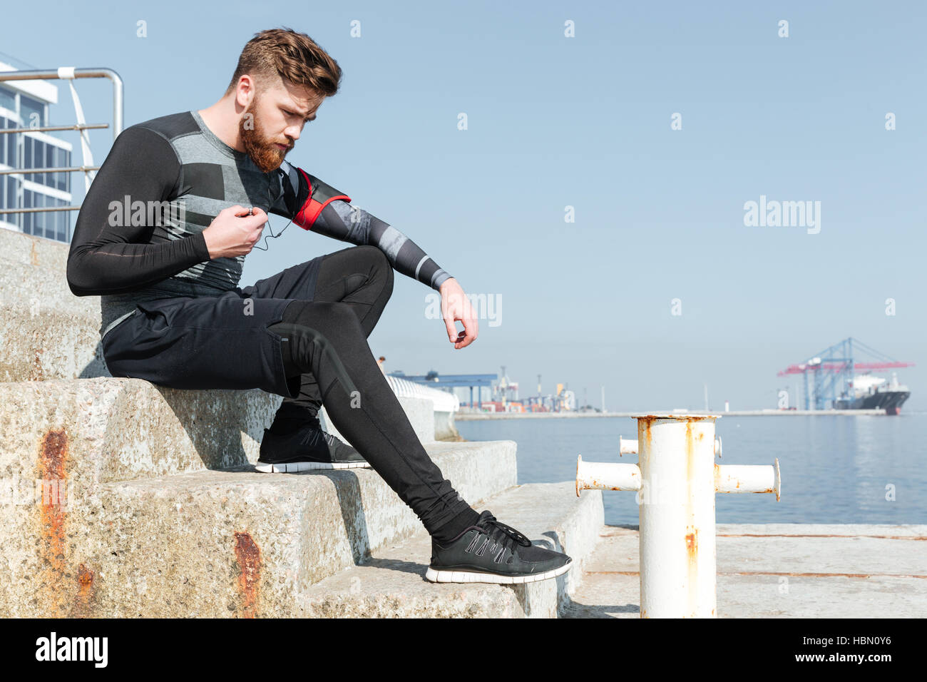 Serious runner sitting on stairs near the sea. looking down. side view ...