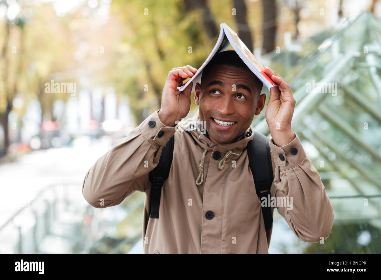 Photo of young happy african man with notebook on his head outdoors ...