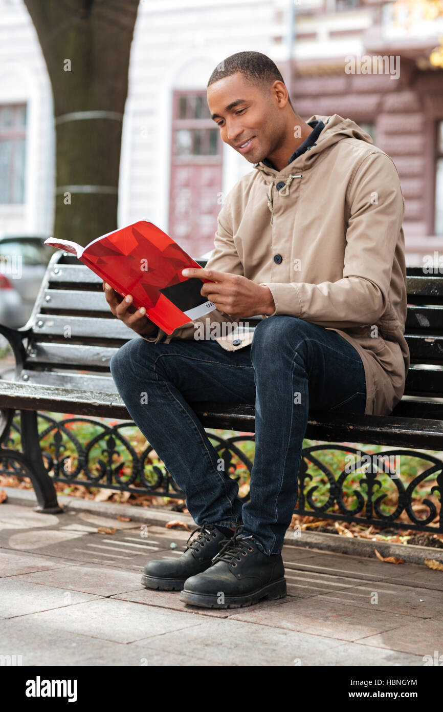 Photo of young african happy man reading a book while sitting on the ...