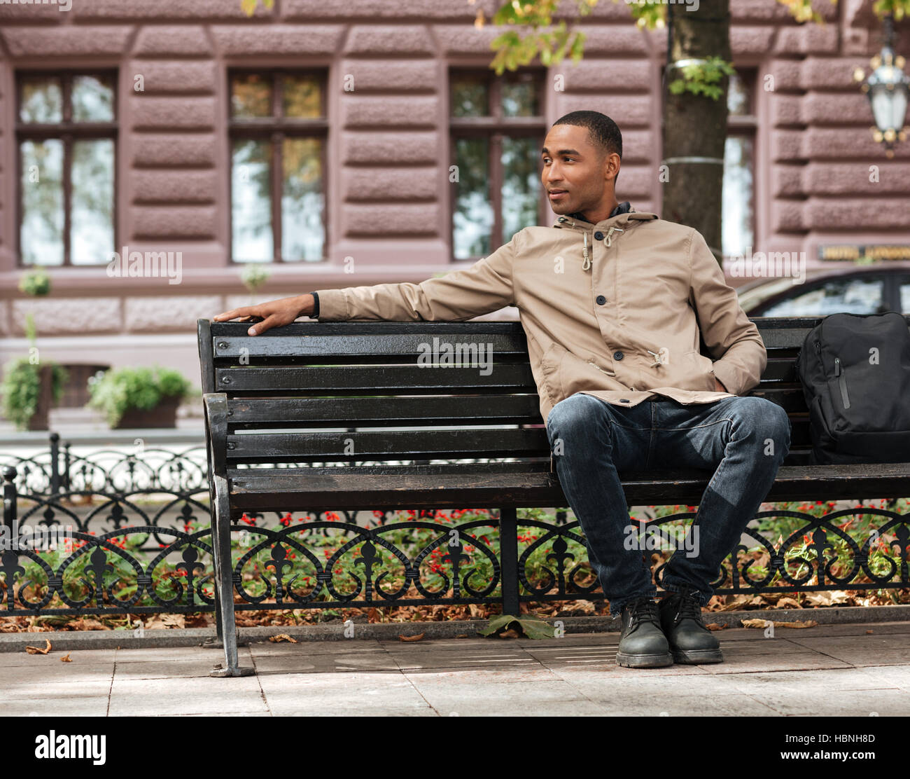 Picture of african happy man sitting on wooden bench near backpack ...