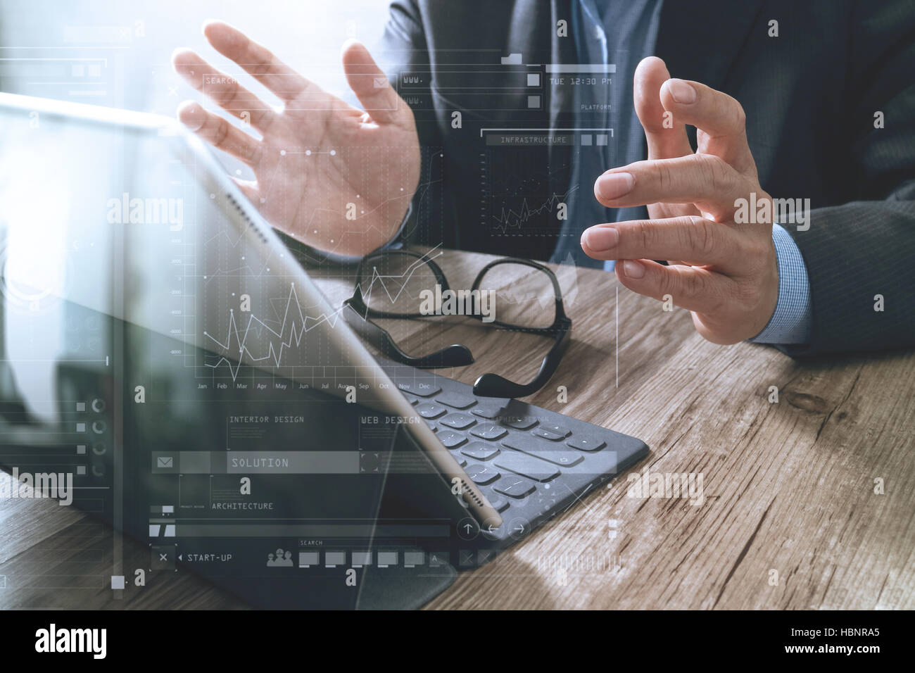 success businessman hand using eyeglass,digital tablet docking smart keyboard on wood desk,icons ...