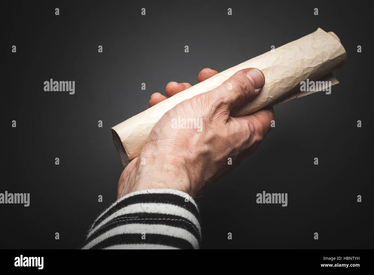 Strong sailor hand holds rolled old crumpled paper sheet over black ...