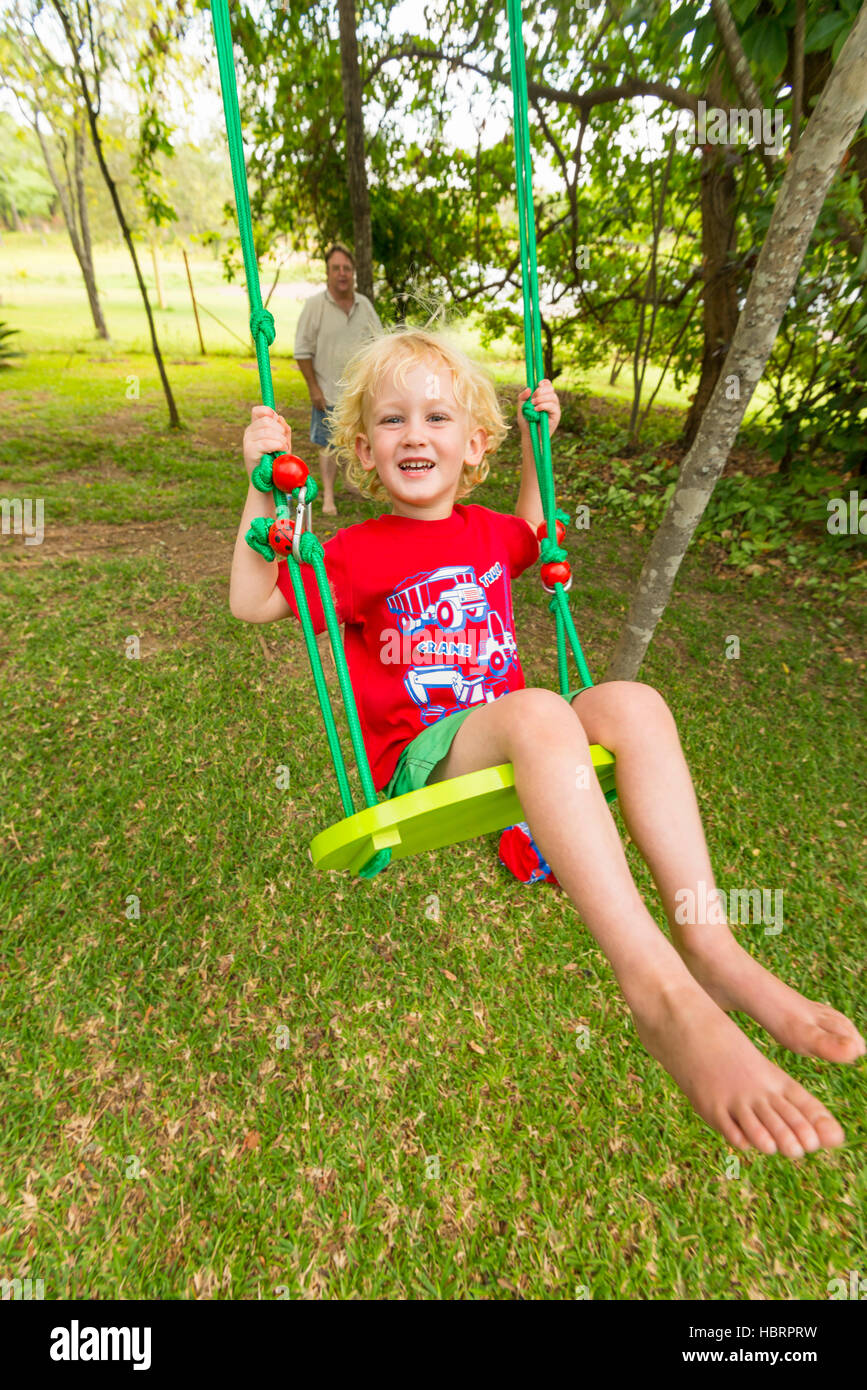A young child being pushed on a swing by his grandfather Stock Photo ...