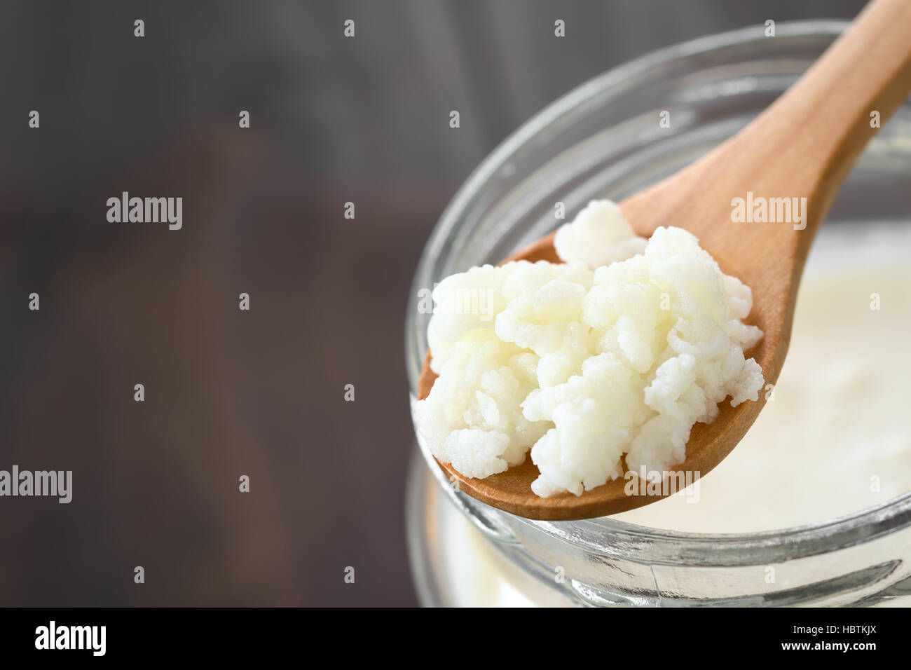 Milk kefir grains on wooden spoon on top of a jar of kefir ...