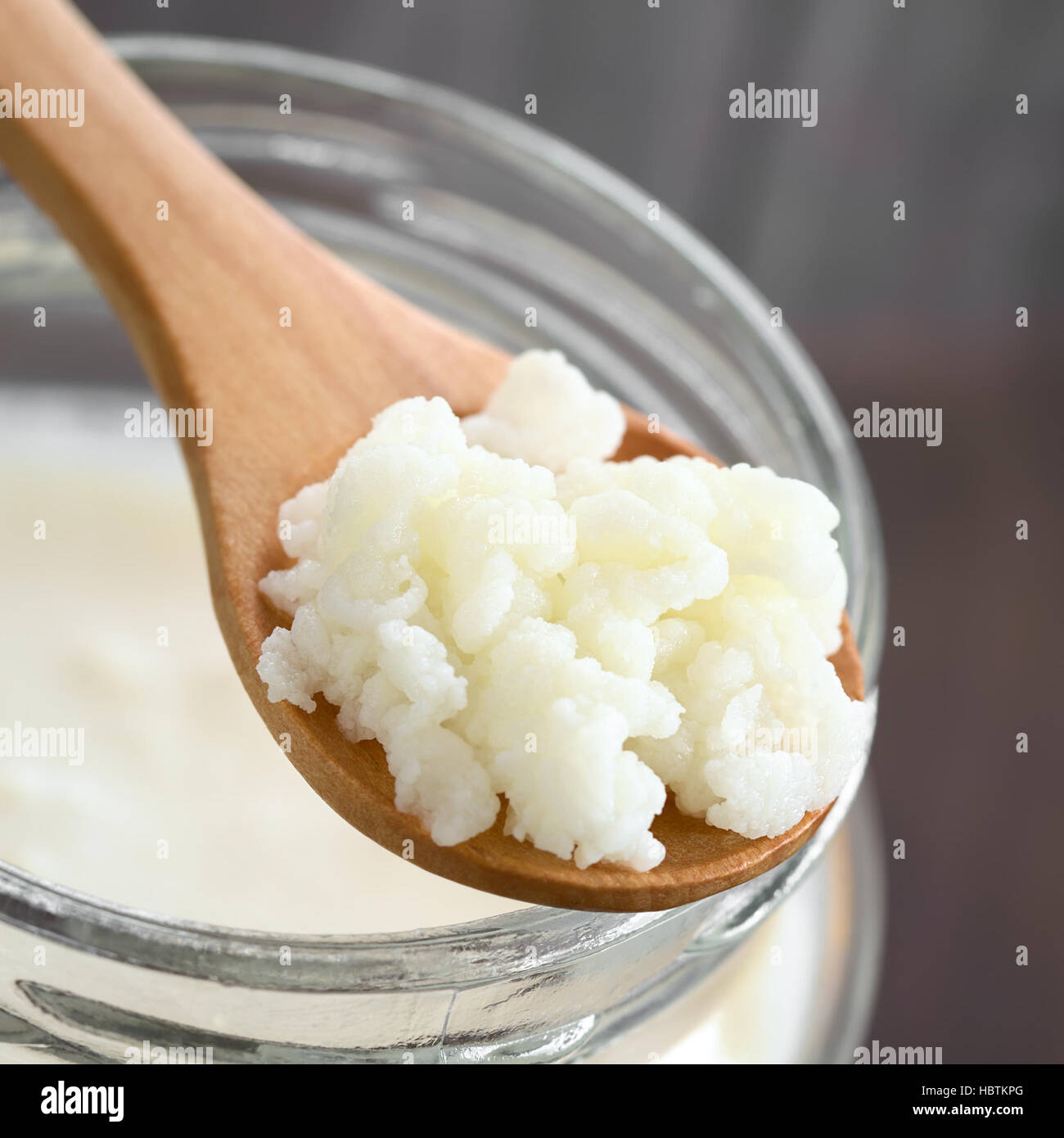 Milk kefir grains on wooden spoon on top of a jar of kefir ...