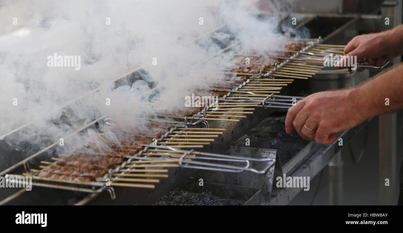 cook prepares skewers of grilled meat with a lot of smoke in a street ...
