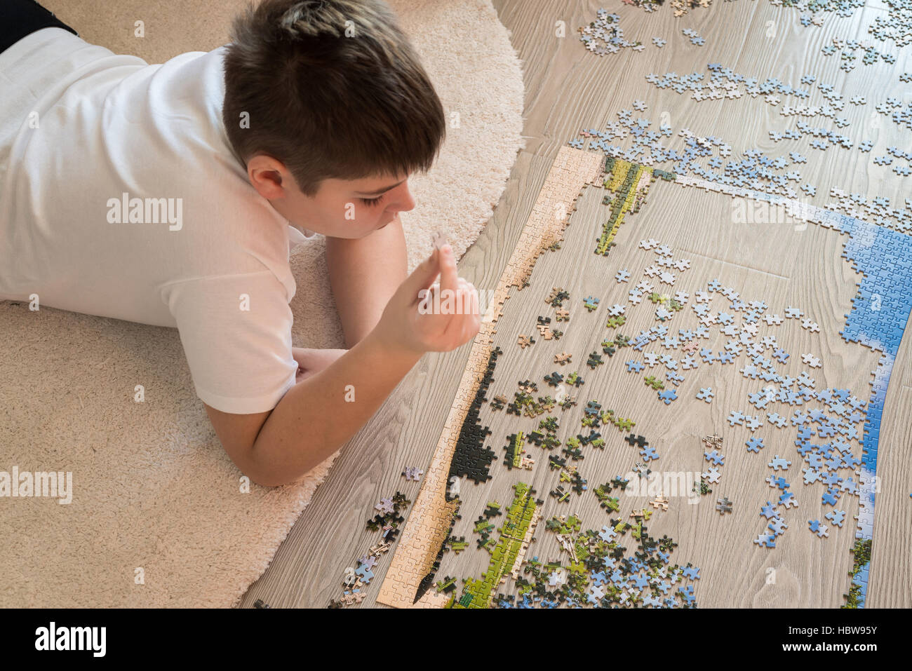 Teen boy collects a puzzle lying on carpet Stock Photo - Alamy