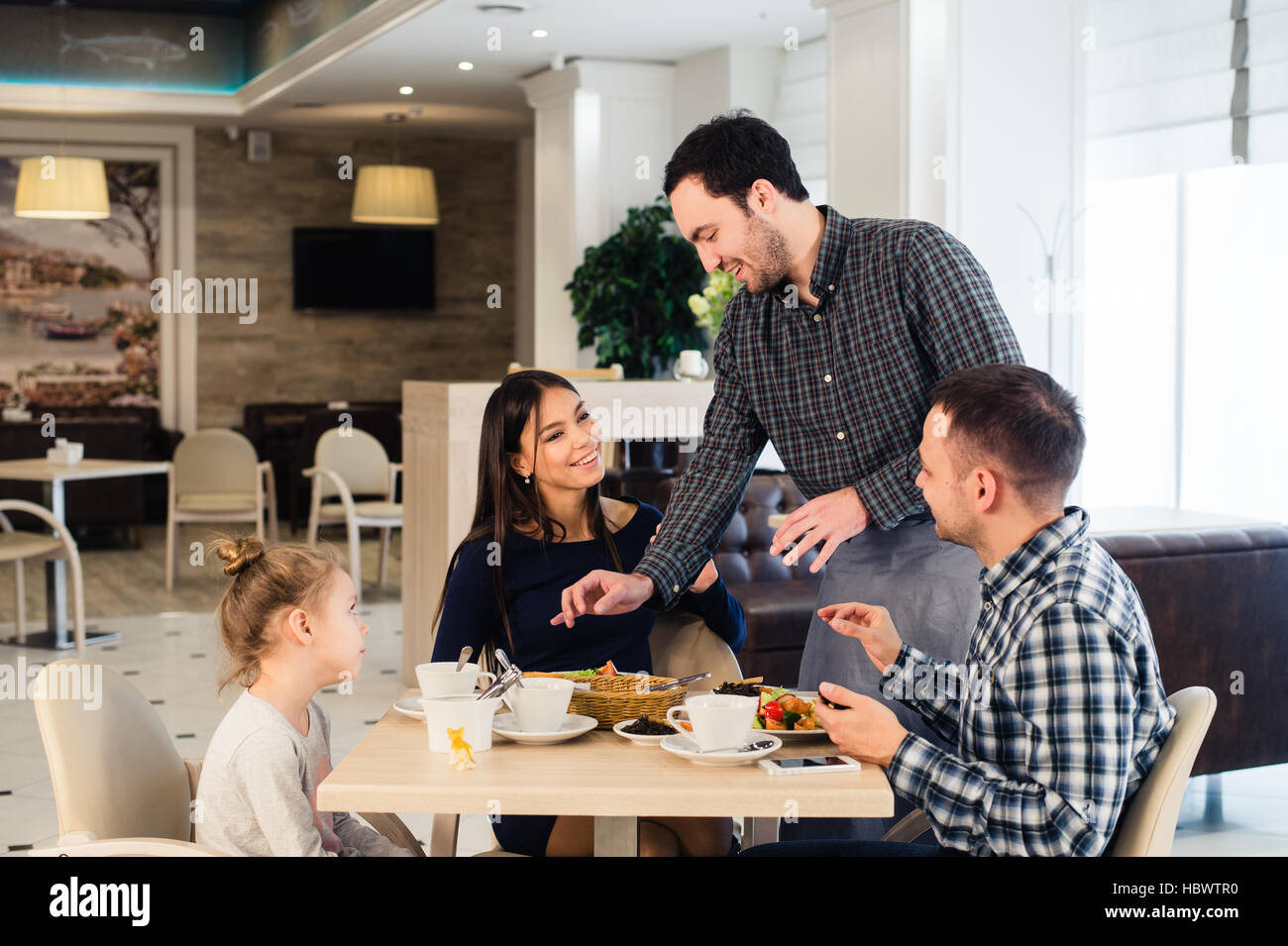 Friendly smiling waiter taking order at table of family having dinner ...
