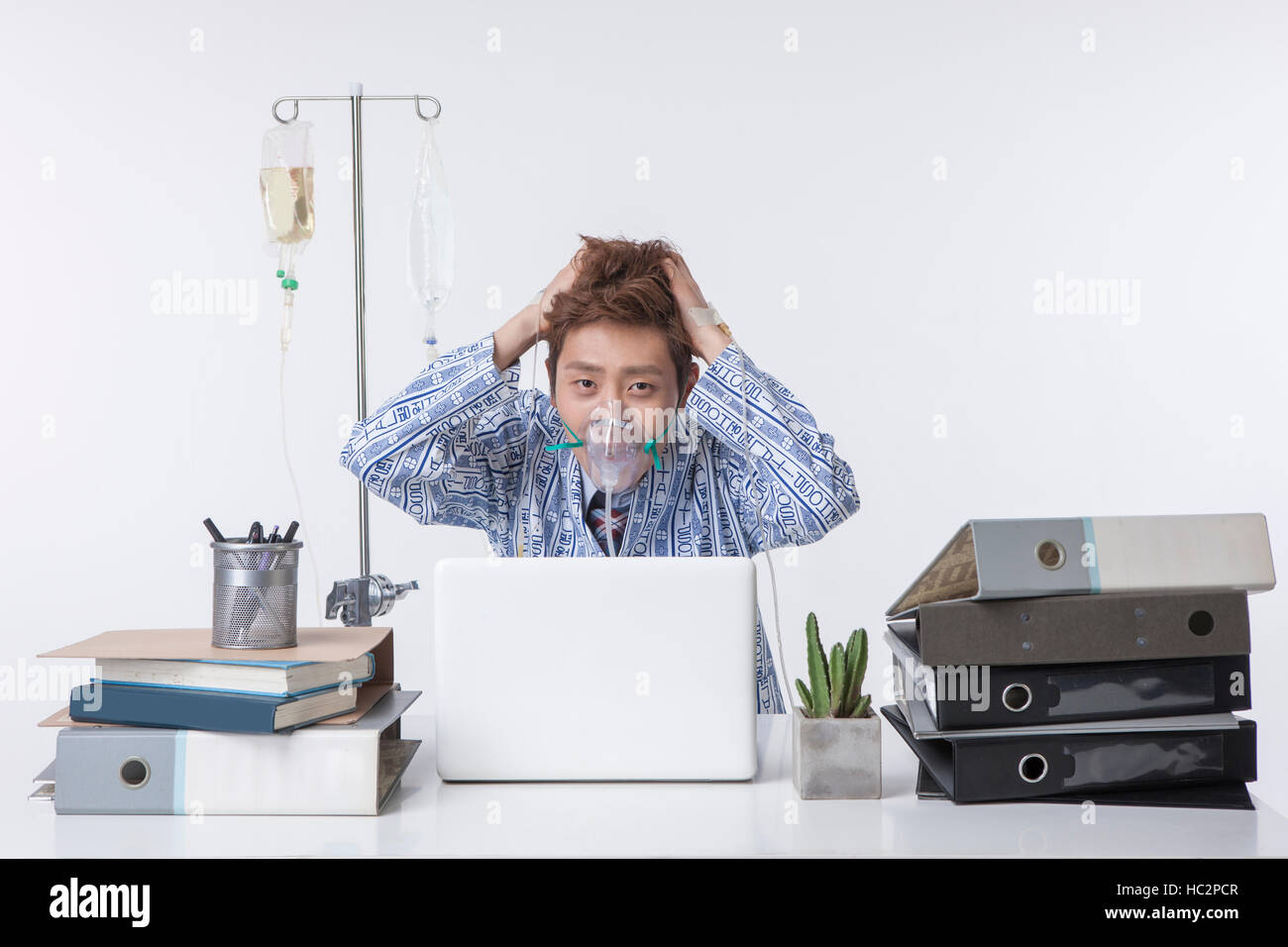 Stressful young businessman in patient's clothes getting an IV at work ...