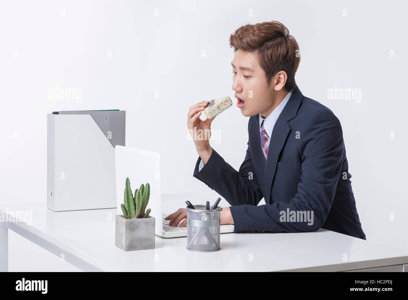 Young businessman using notebook computer eating a riceball at work ...