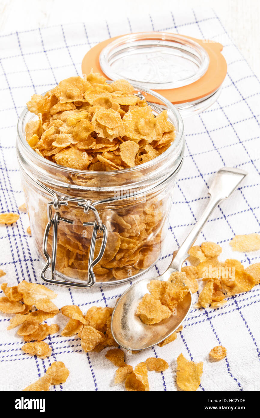 cornflakes in a glass storage container with spoon on a blue and white ...