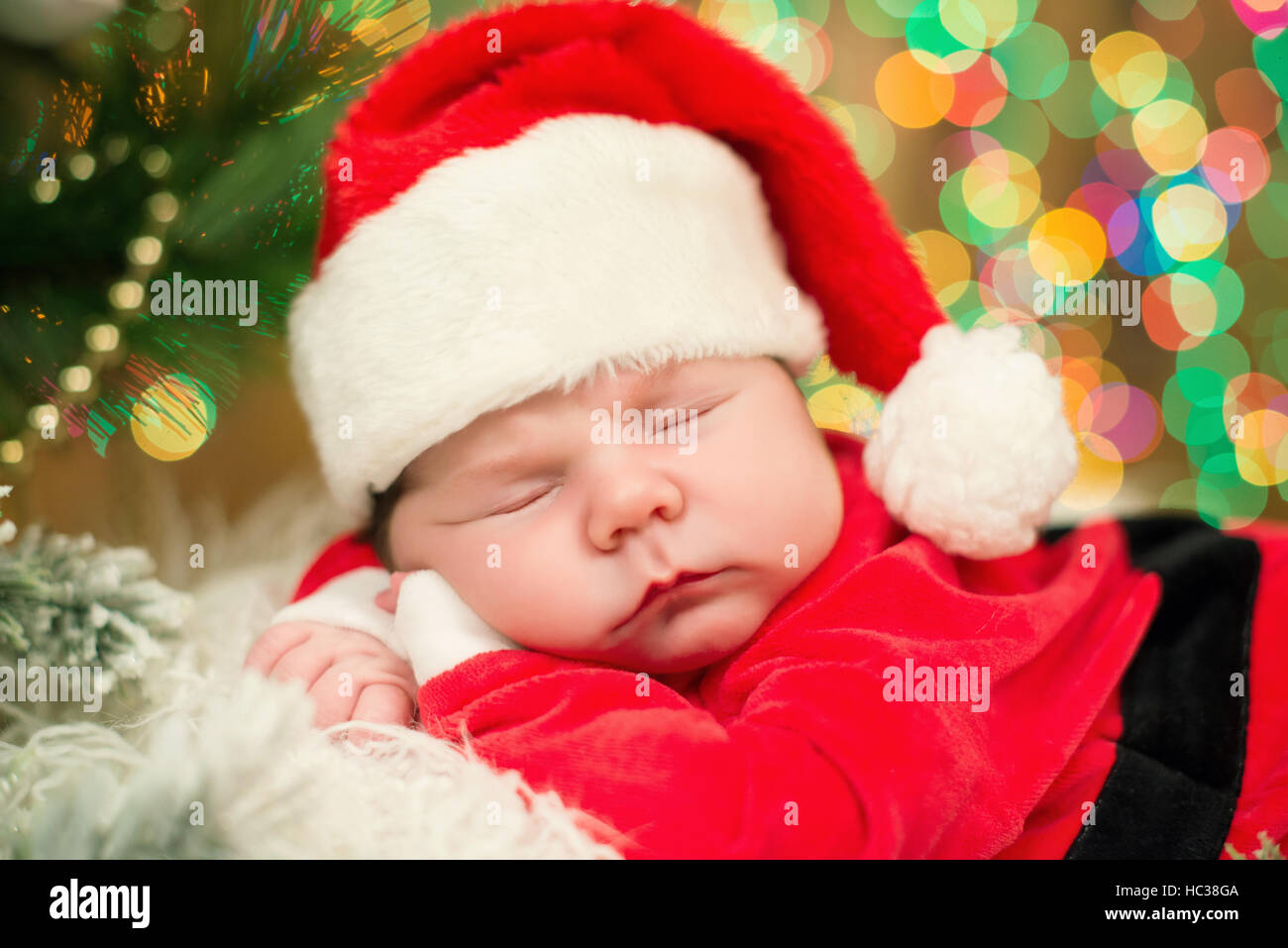Portrait of newborn baby in Santa clothes lying under Christmas tree ...