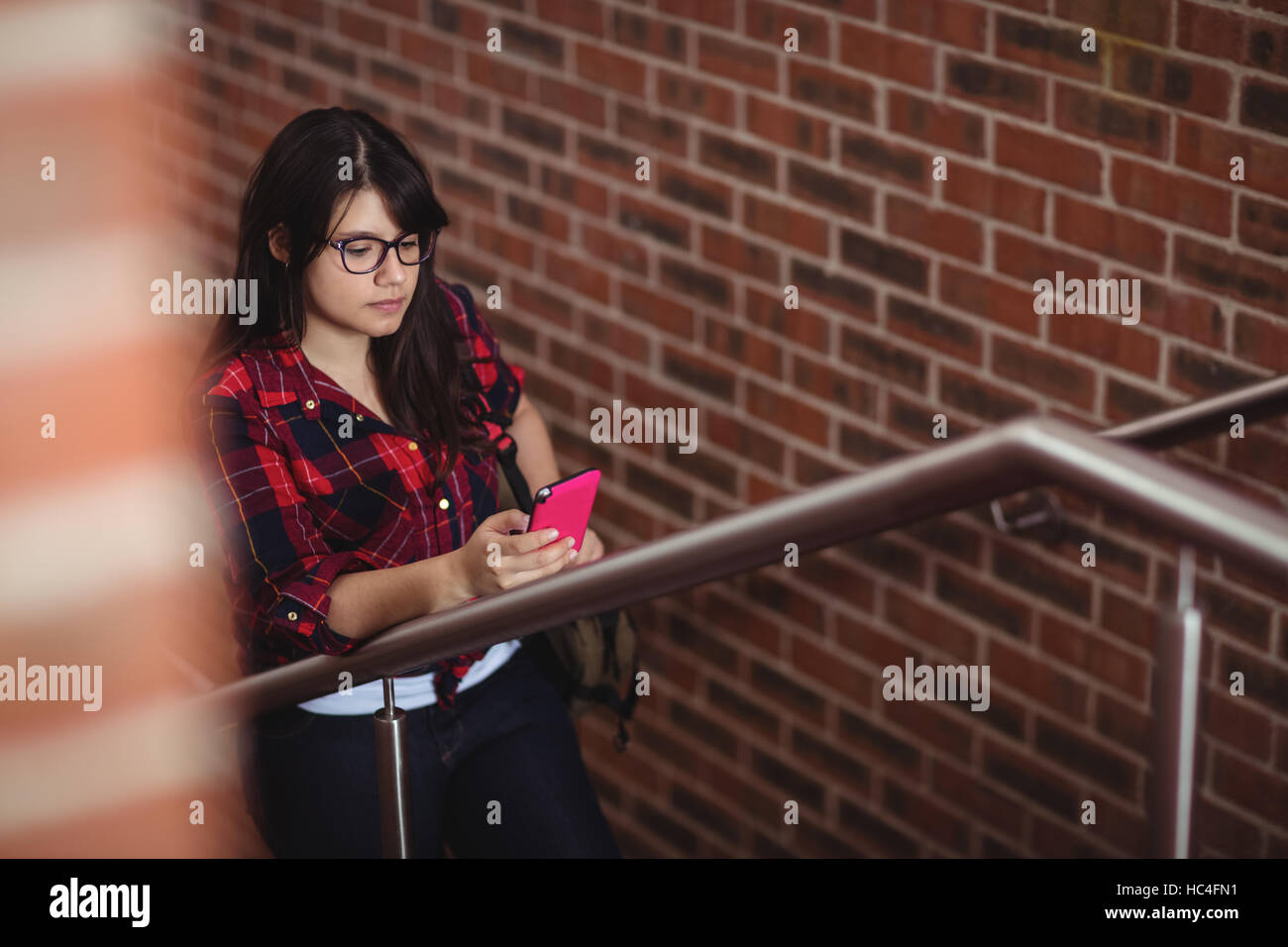 Female student walking on staircase while using mobile phone Stock ...