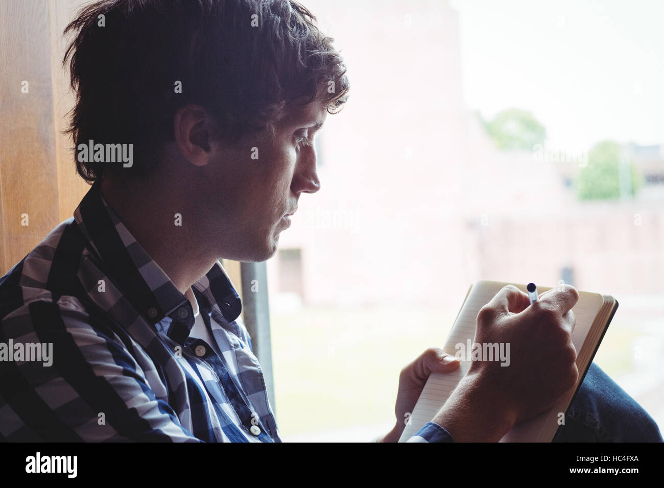 Student writing notes near window Stock Photo - Alamy