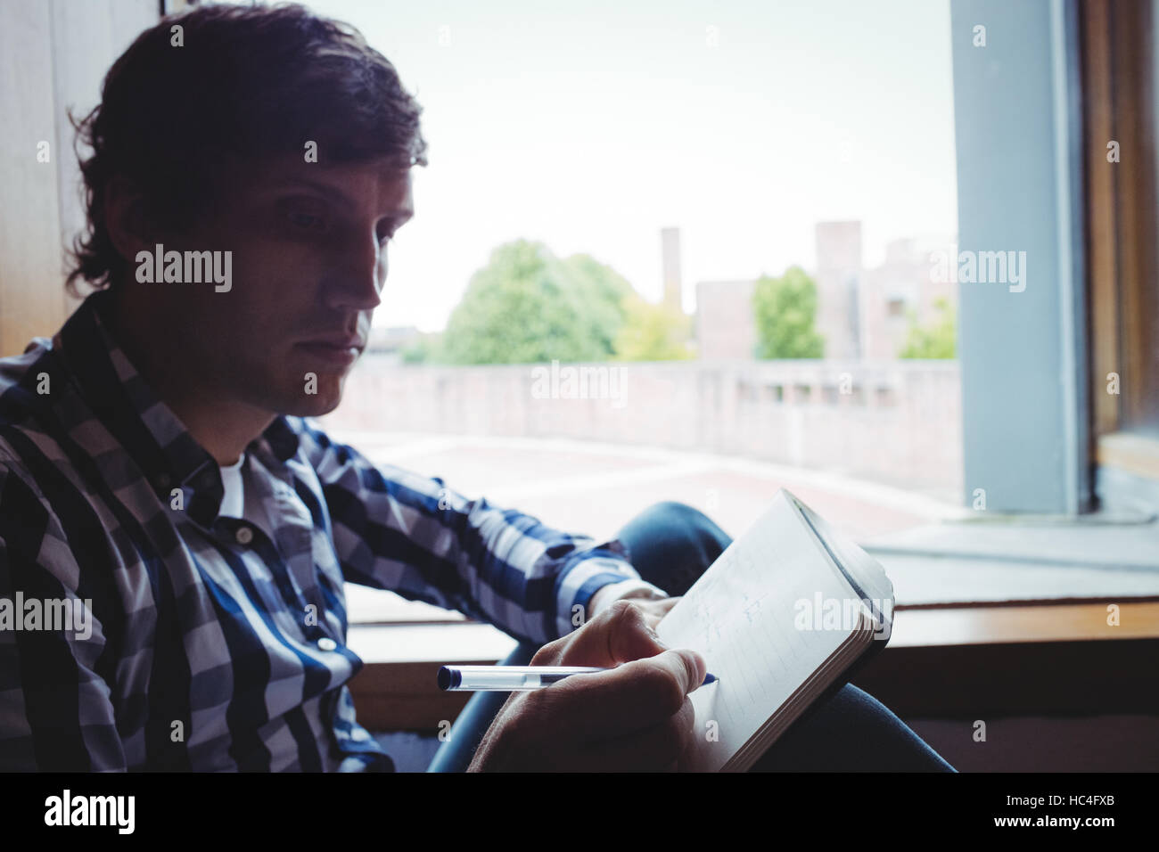 Student writing notes near window Stock Photo - Alamy