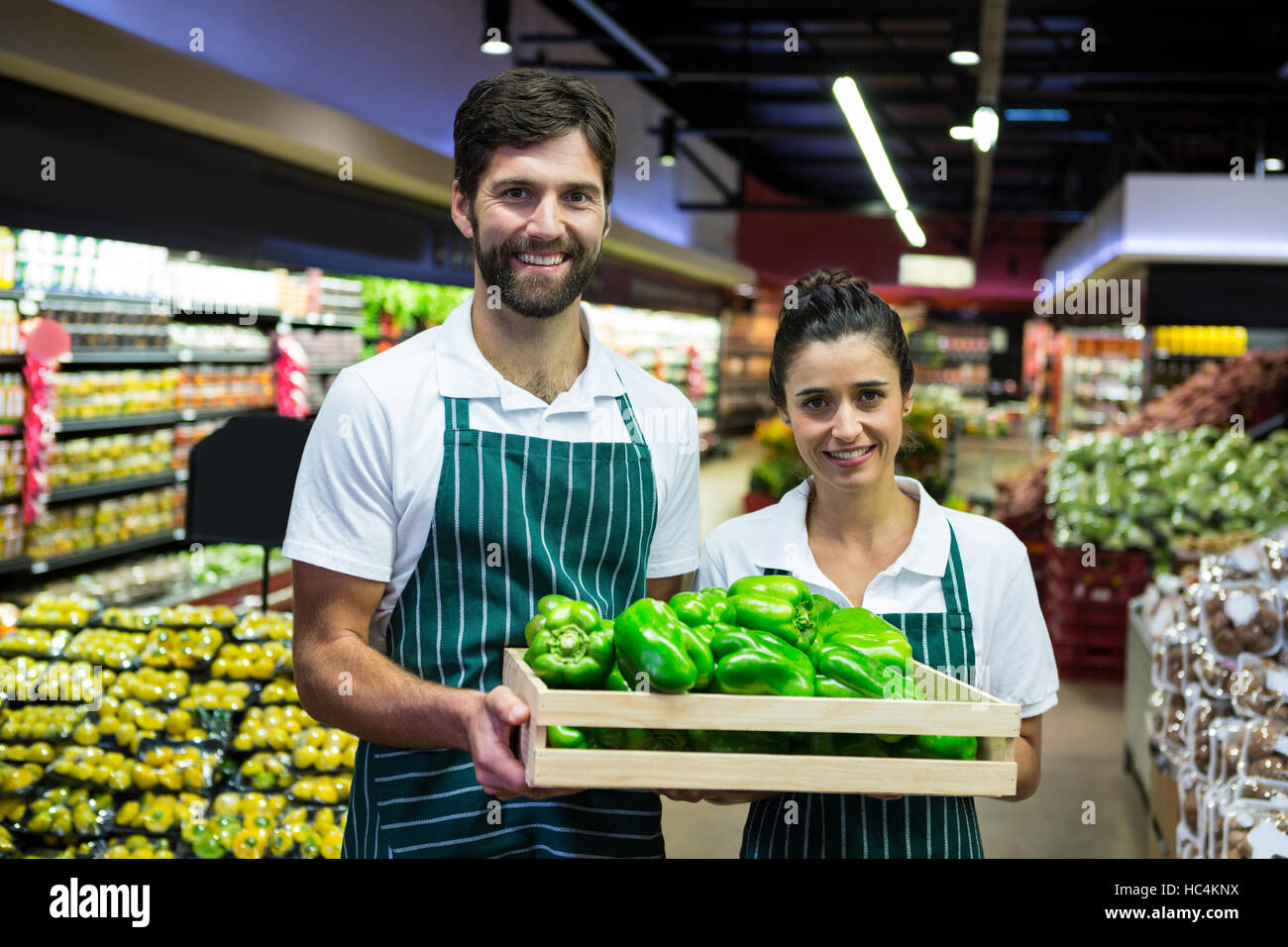 Smiling staff holding a crate of green bell pepper at supermarket Stock ...