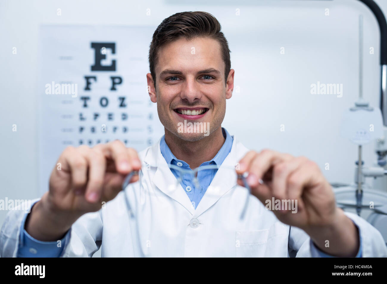 Smiling optometrist holding spectacles Stock Photo - Alamy