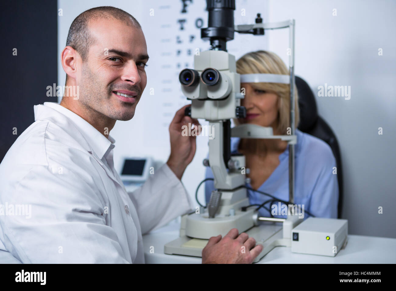 Smiling optometrist examining female patient on slit lamp Stock Photo ...