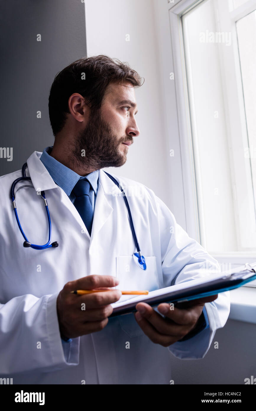 Doctor looking through window while holding clipboard Stock Photo - Alamy