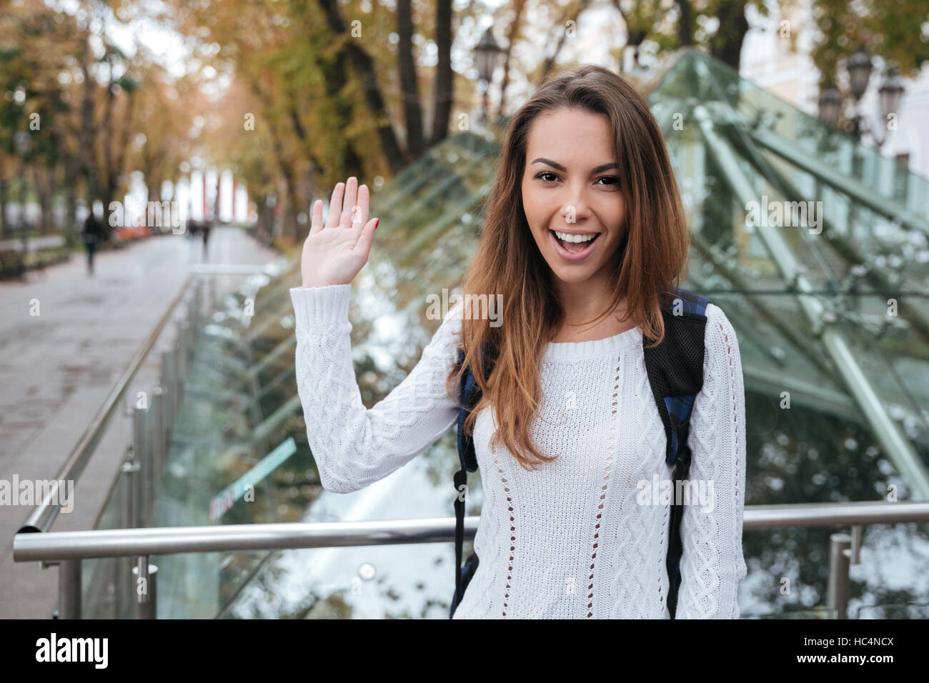 Smiling beautiful young woman waving and saying hello to you in park ...