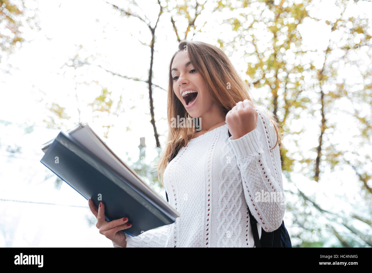 Cheerful excited young woman with notebook shouting and celebrating ...