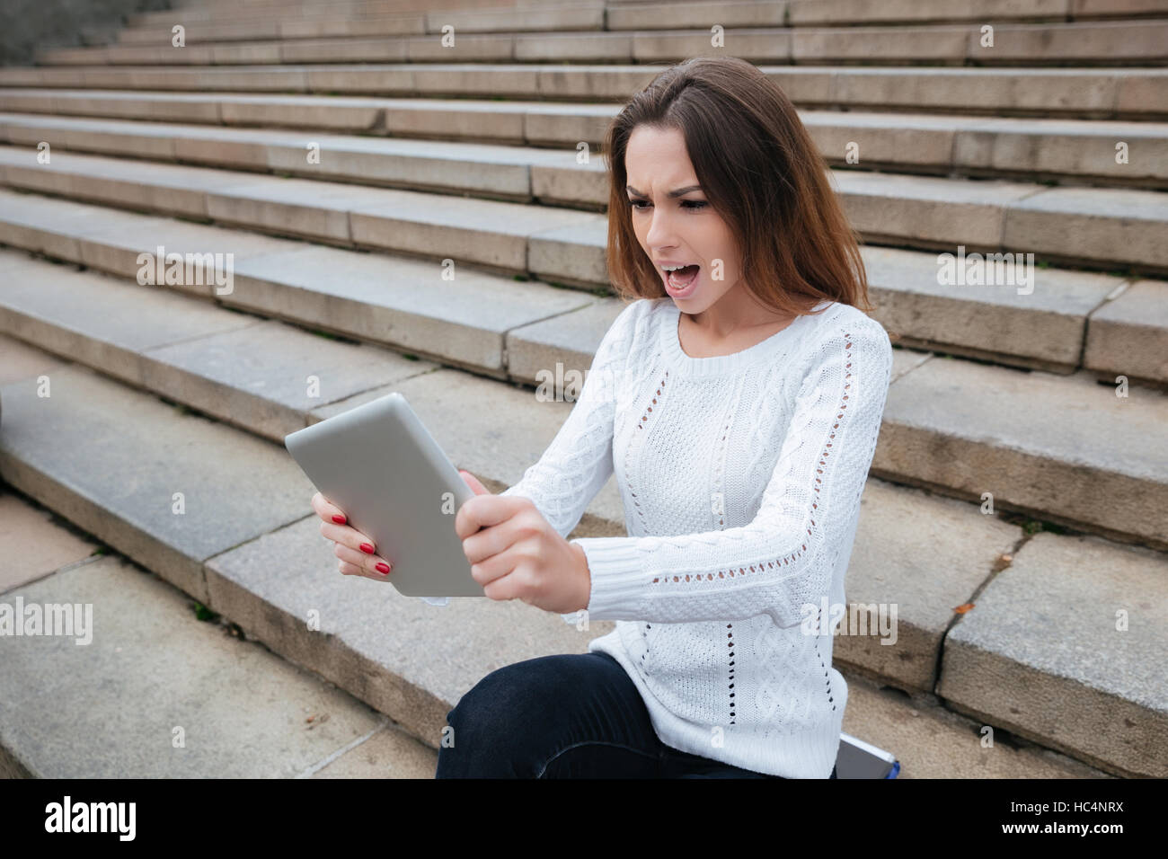 Angry pretty young woman sitting on stairs and using tablet Stock Photo ...