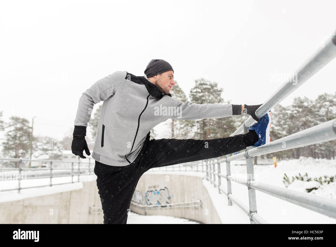 sports man stretching leg at fence in winter Stock Photo - Alamy